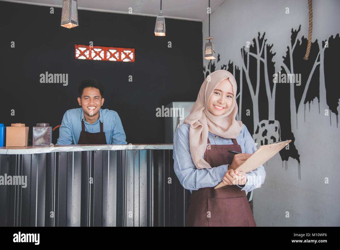 Happy asian male waiter using apron writing order. muslim entrepreneur ...