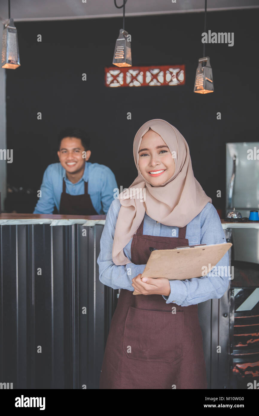 Happy asian male waiter using apron writing order. muslim entrepreneur ...