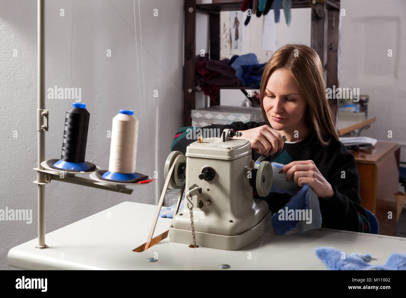 Sewing process of the female fur coat. A young cheerful woman furrier ...