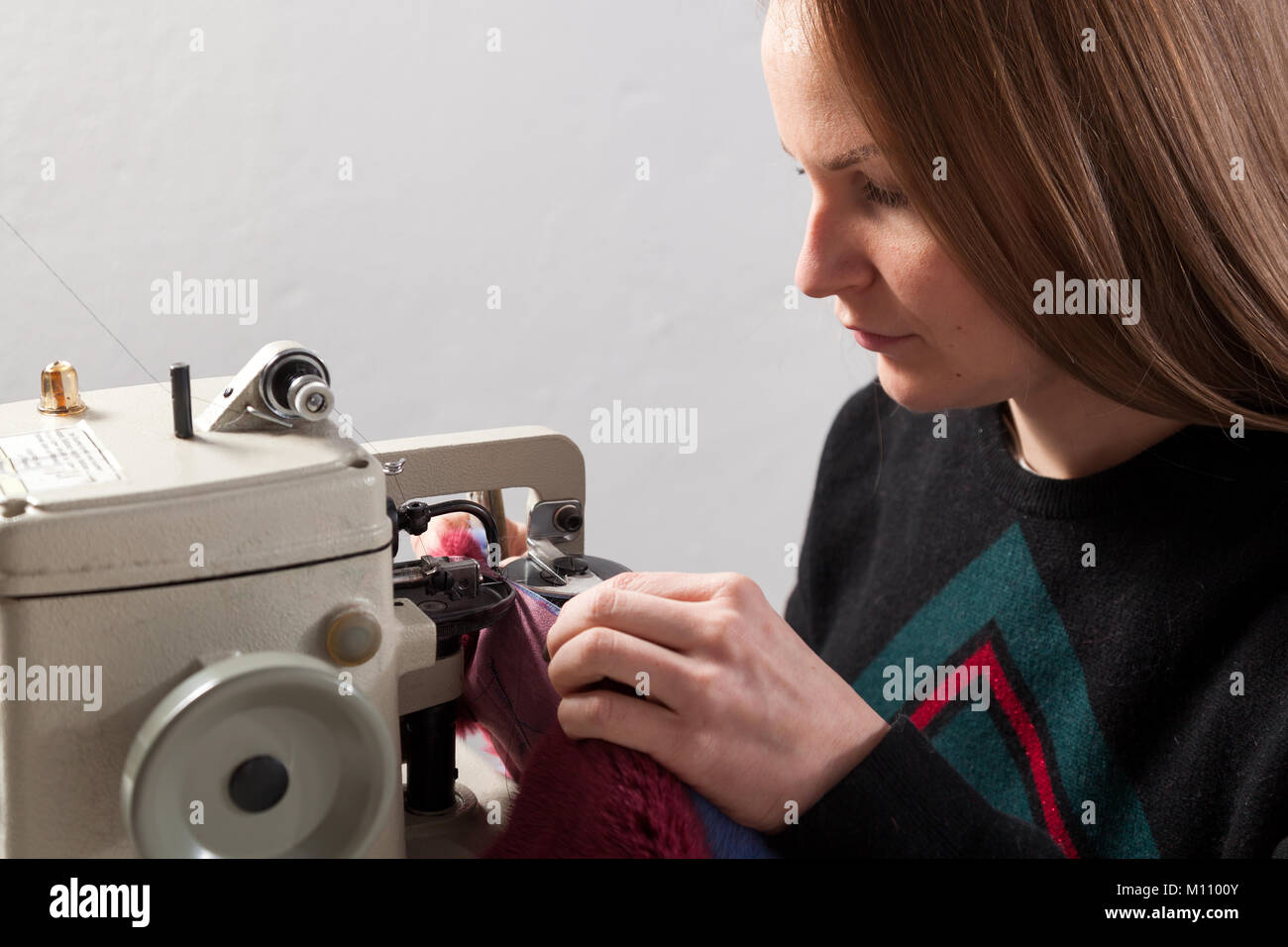 A young woman scinner, furrier sews a bright fur coat of natural blue ...
