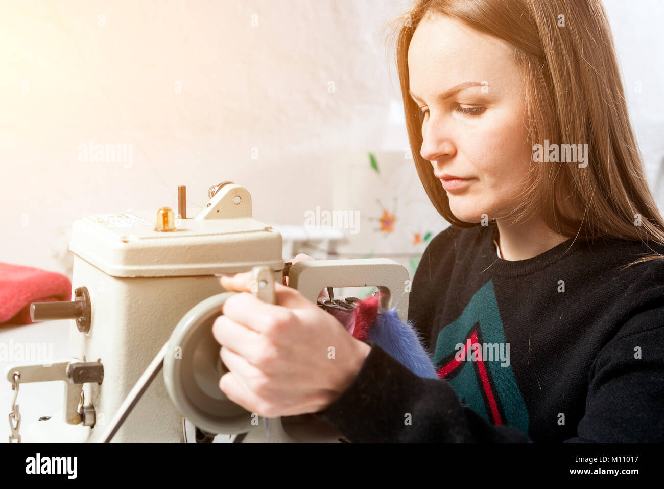 A young woman scinner, furrier looks closely and sews a bright fur coat ...