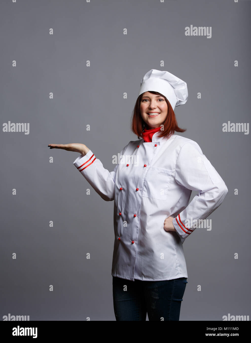 Image of smiling brunette chef in white robe with empty palm on gray ...