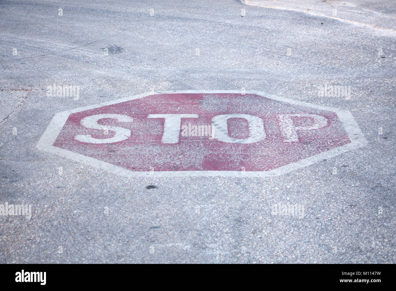 Weathered red hexagon stop sign painted on roads pavement surface ...