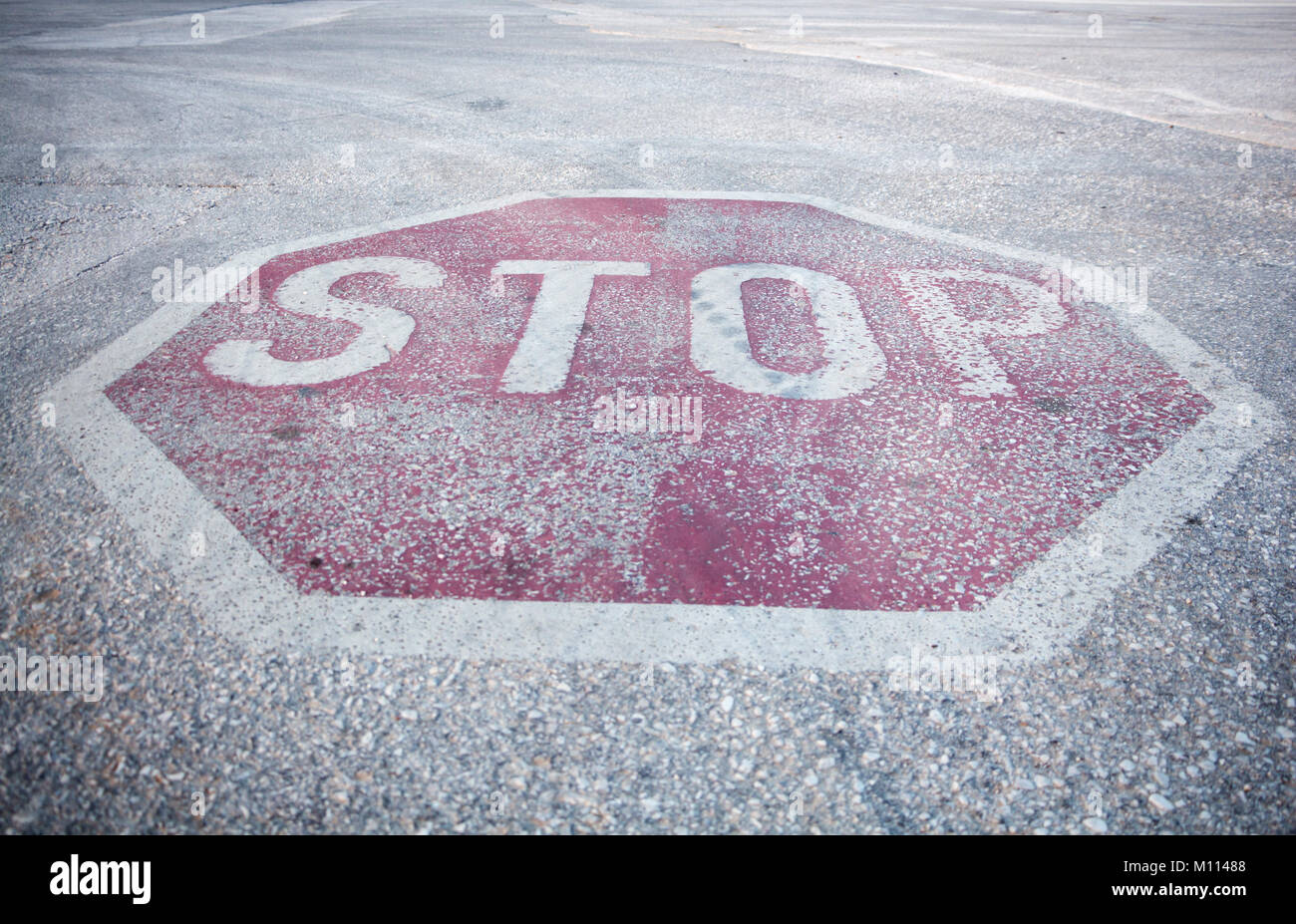 Weathered red hexagon stop sign painted on roads pavement surface ...