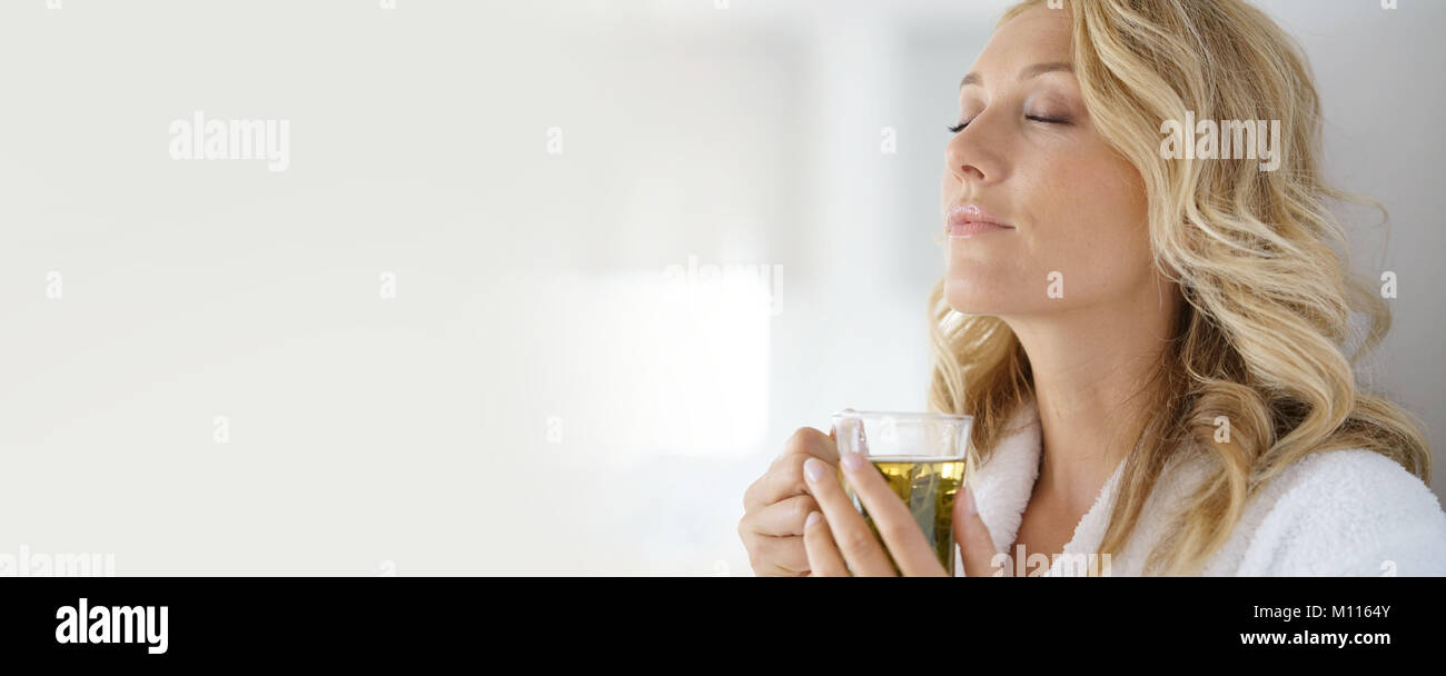 Portrait of attractive 40-year-old woman in bathrobe drinking infusion ...