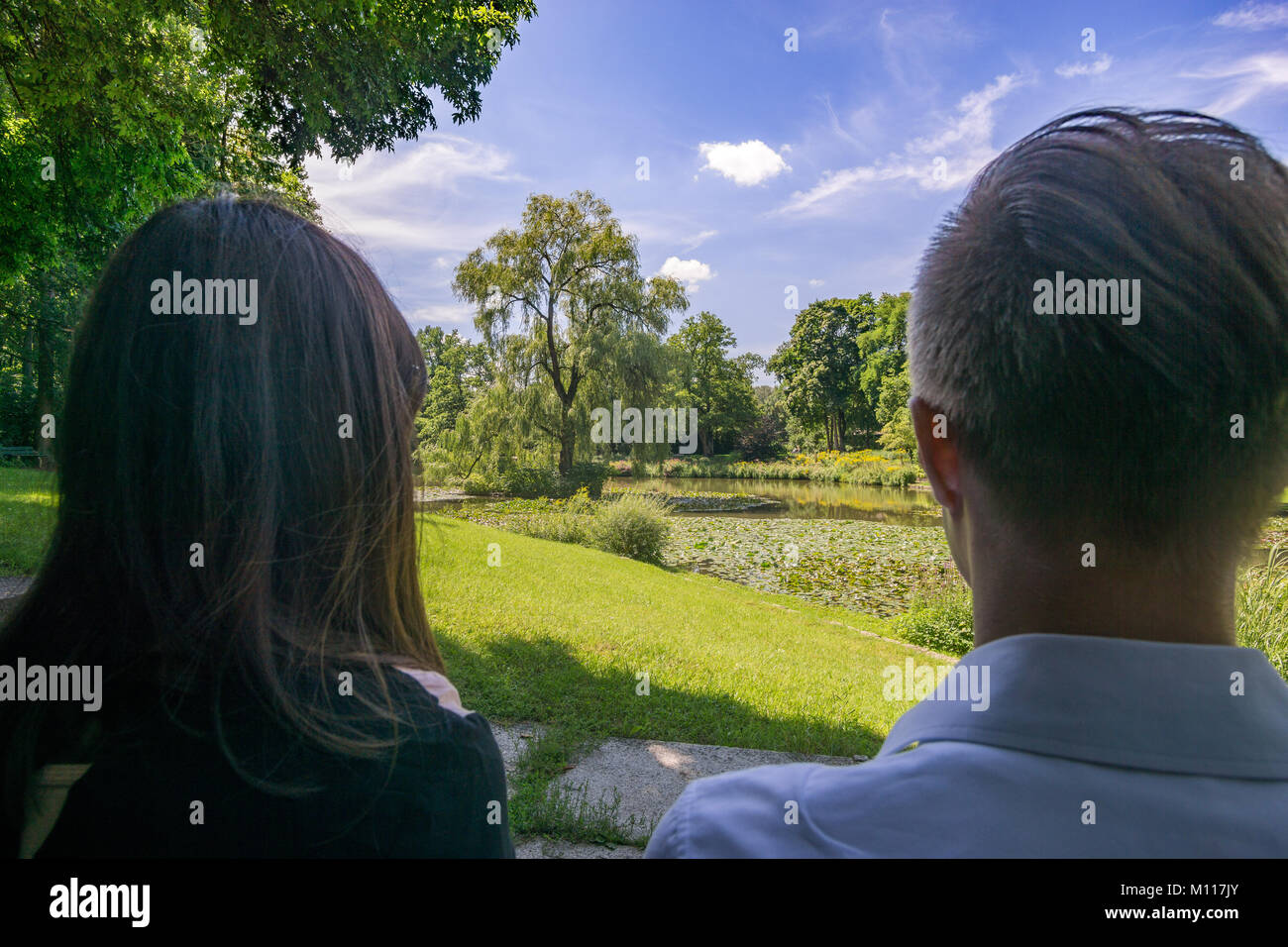 Young Couple from the back sitting together on a bench in the shadow ...