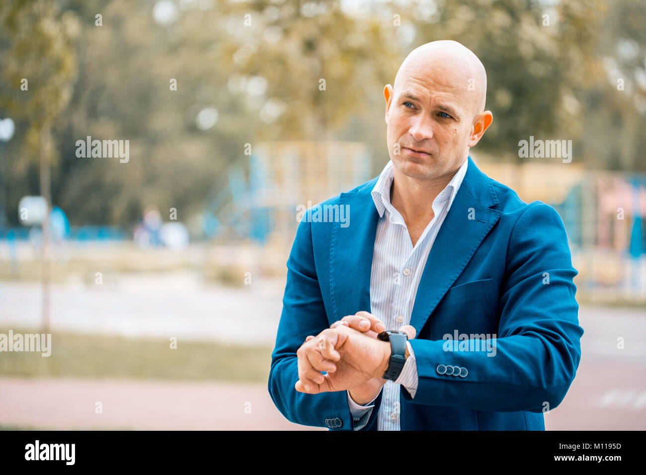 Serious male bald entrepreneur in formal suit looking at wristwatch ...
