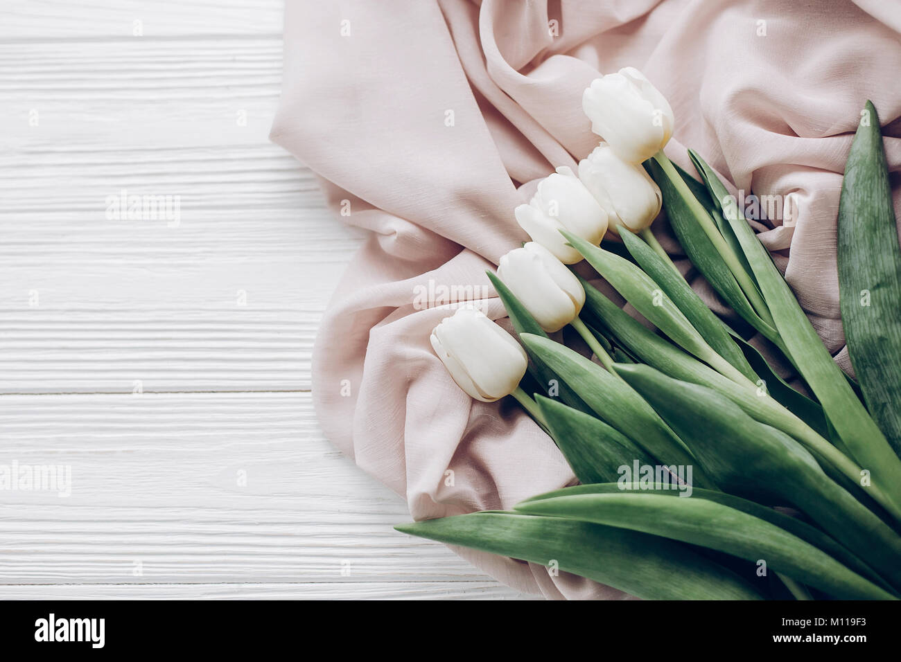 stylish white tulips on beige soft fabric and rustic wooden table ...