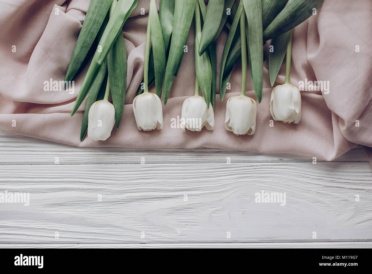 stylish white tulips on beige soft fabric and rustic wooden table ...