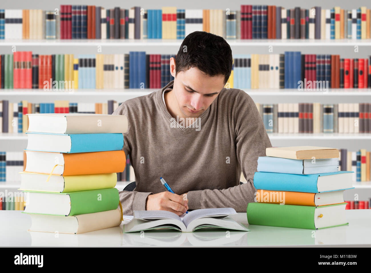 Young Male University Student Studying In Front Of Bookshelf At Library ... Young Male University Student Studying In Front Of Bookshelf At Library ...