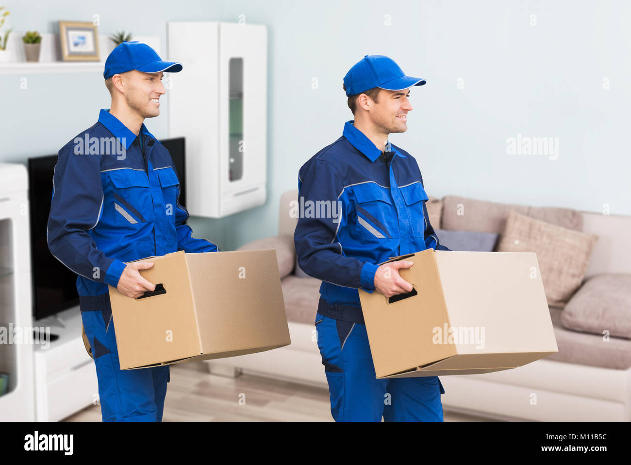 Young Smiling Professional Movers In Uniform Delivering Cardboard Boxes ...