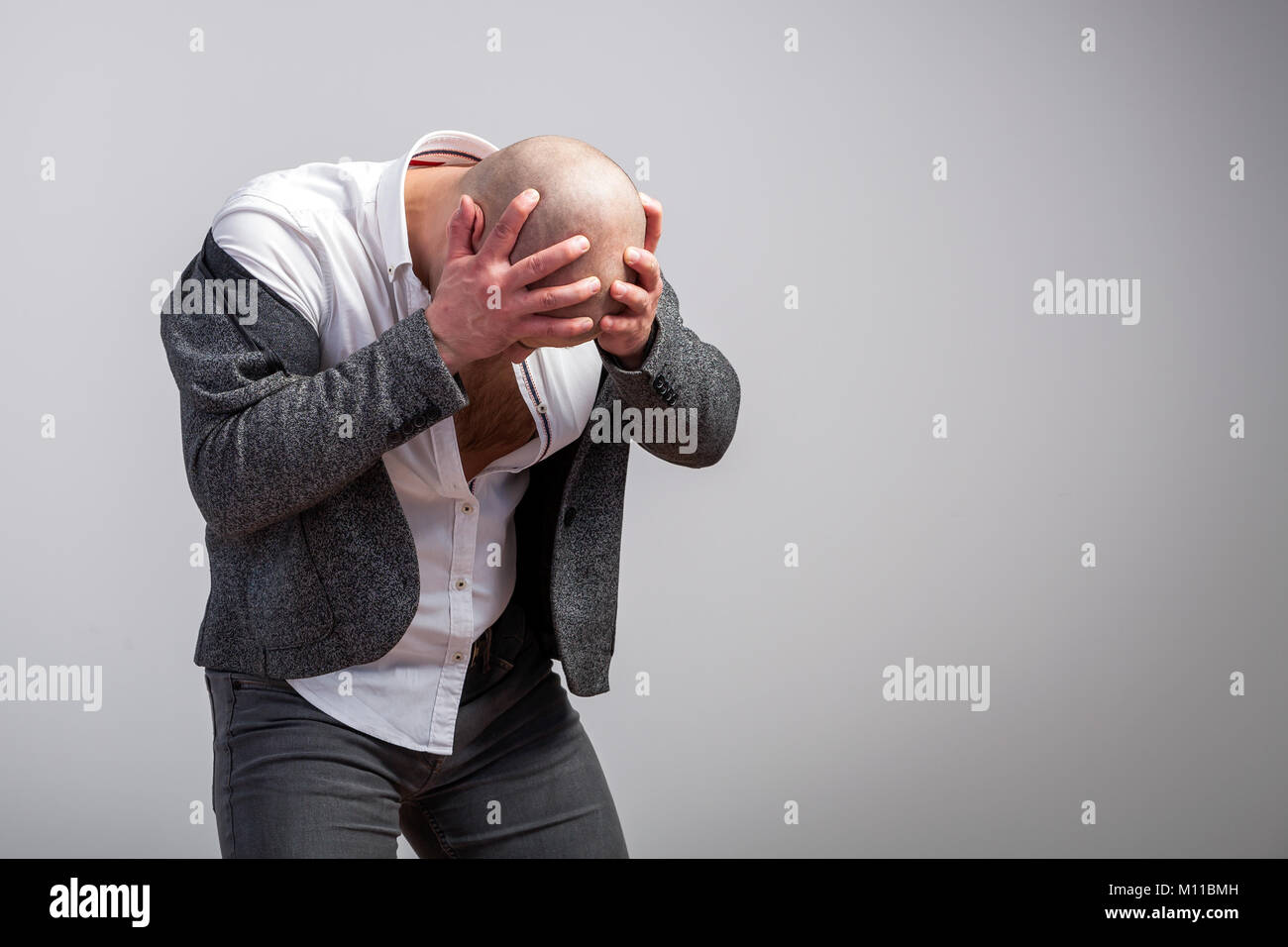 A young bald man in an unbuttoned gray suit and white shirt is upset ...
