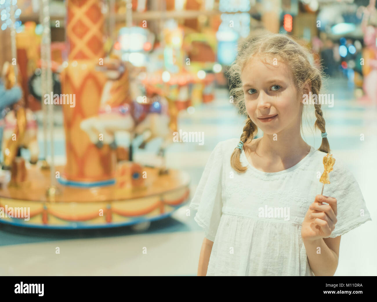 Cute little girl with lollipop in amusement park Stock Photo - Alamy