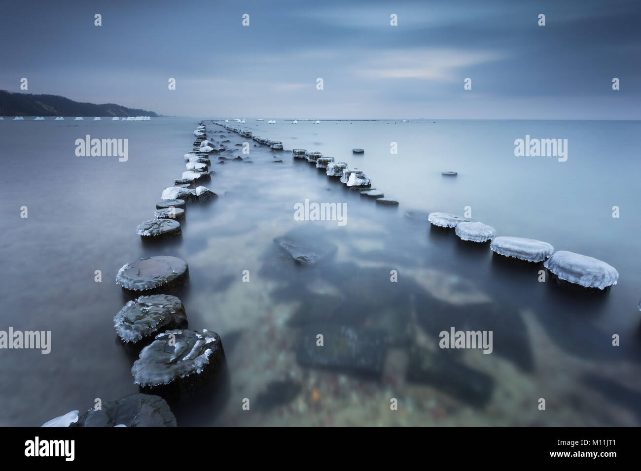 Winter landscape at the sea. Frozen wooden breakwaters line to the ...