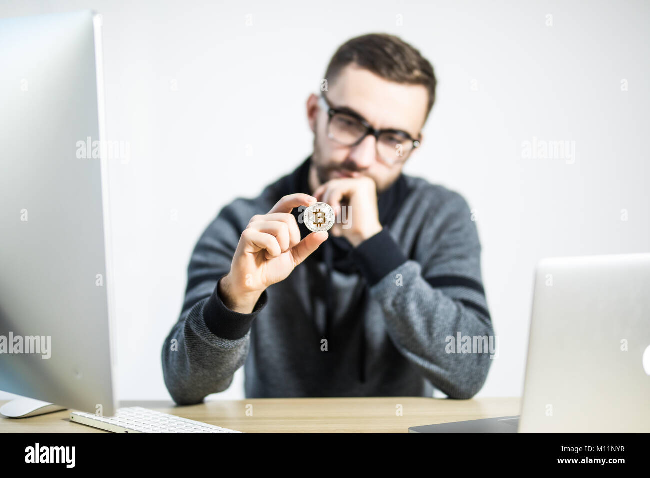 Handsome man thinking over bitcoin at working table with laptop and ...