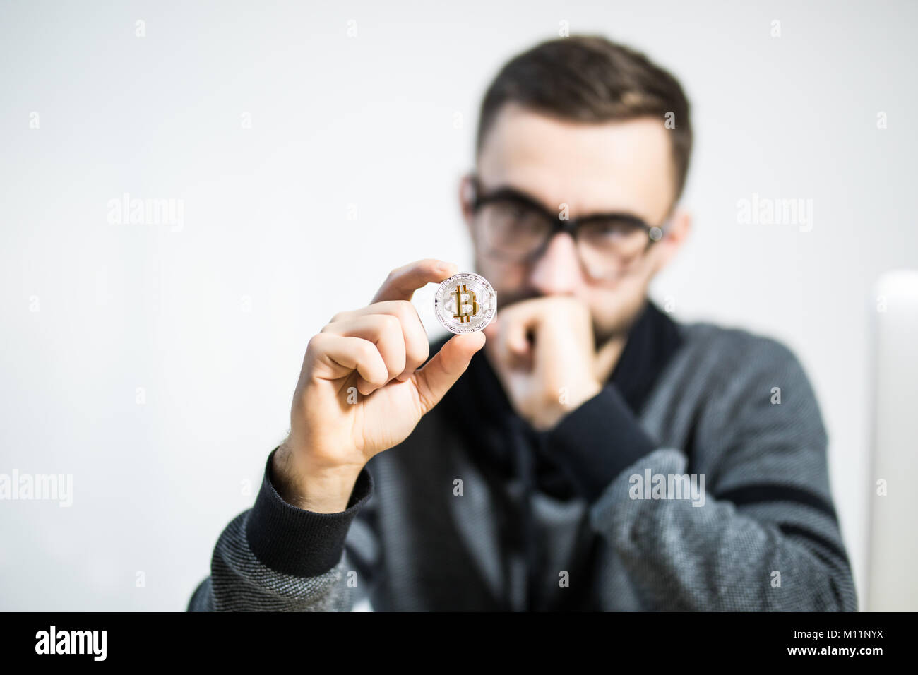 Handsome man thinking over bitcoin at working table with laptop and ...