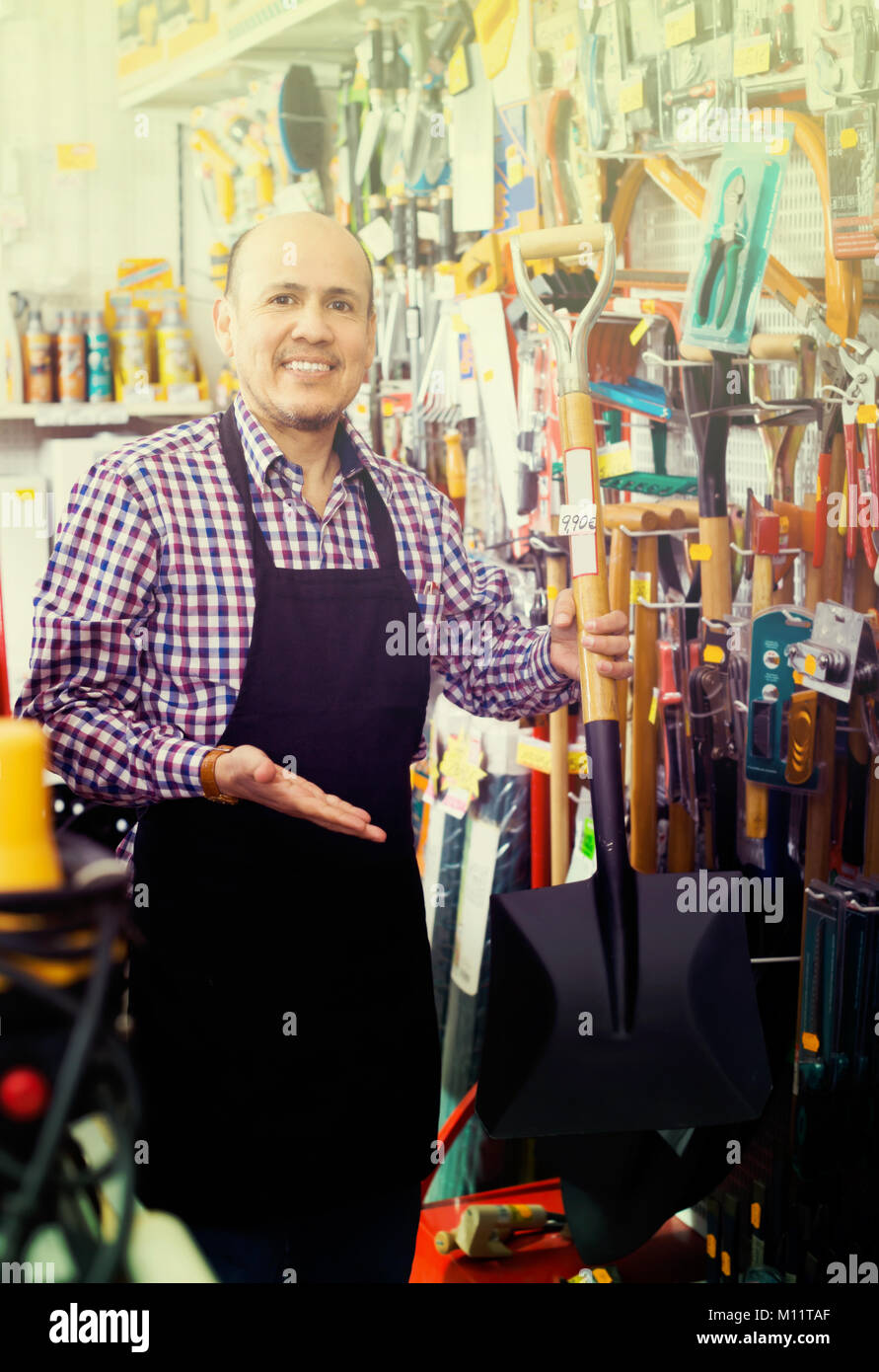 Professional senior salesman offering garden tools in building store ...
