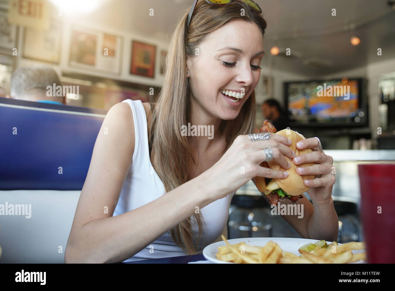Portrait of cheerful girl eating hamburger in fast food restaurant ...