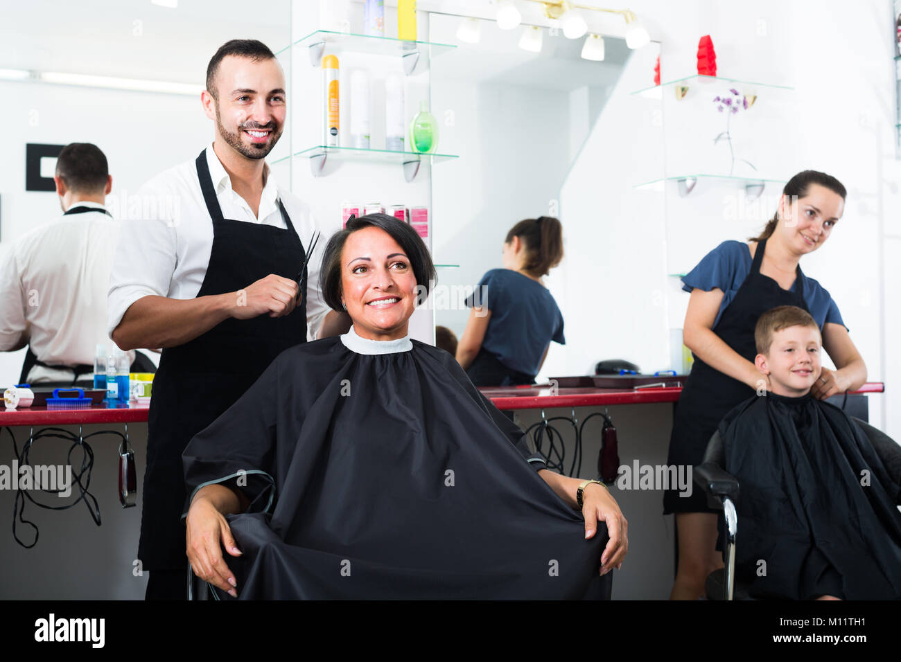 friendly man hairdresser cutting hair of smiling female client in ...