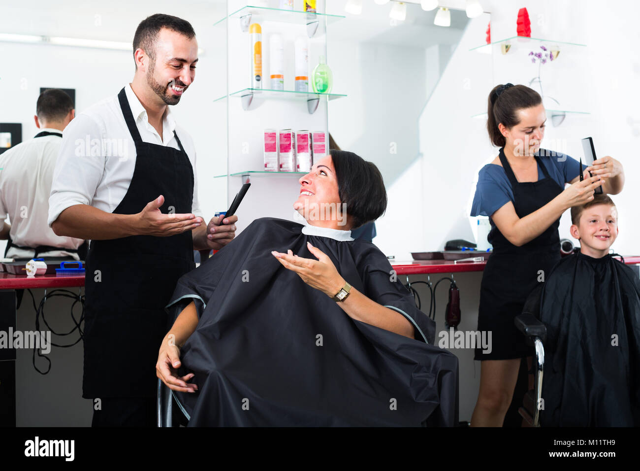 happy man hairdresser talking to woman ready to cut her hair in crowded ...