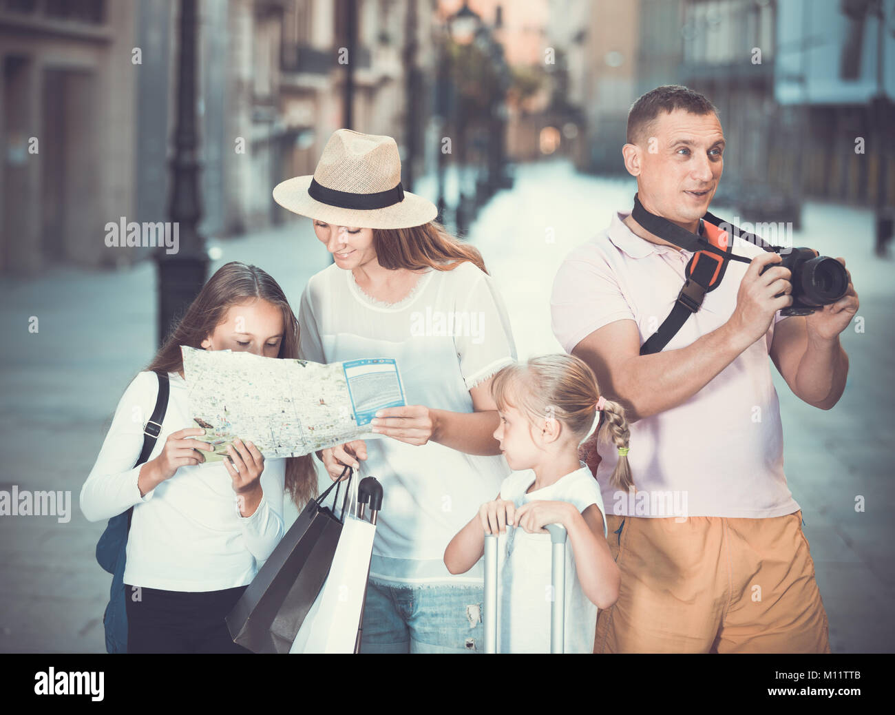 Smiling parents with two kids using map and photographing sights during ...