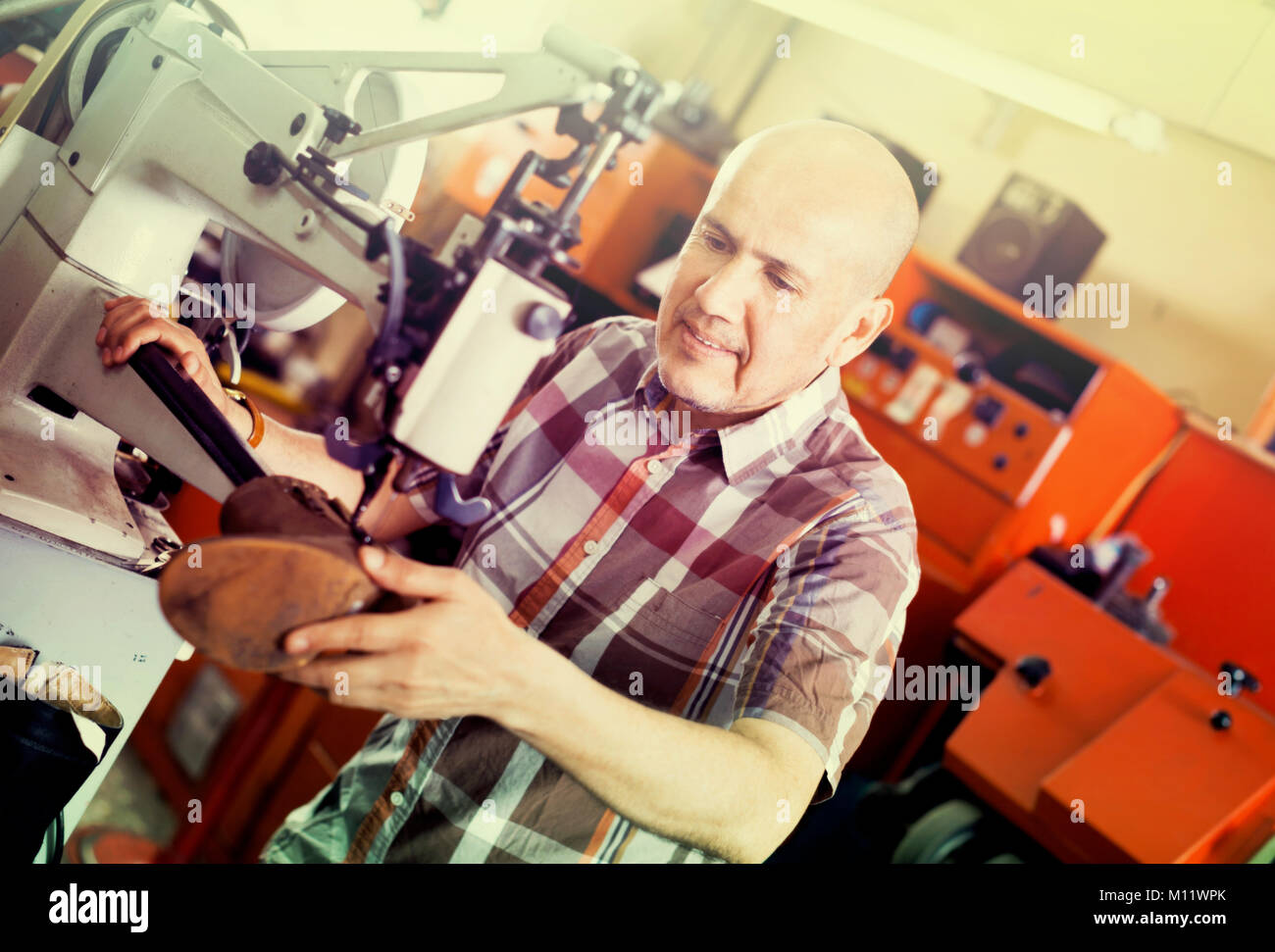 Mature diligent positive workman sewing leather boots on stitch lathe ...