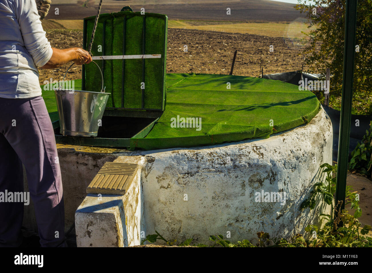 A women drawing water of a pit in a rural eco village in Andalusia ...