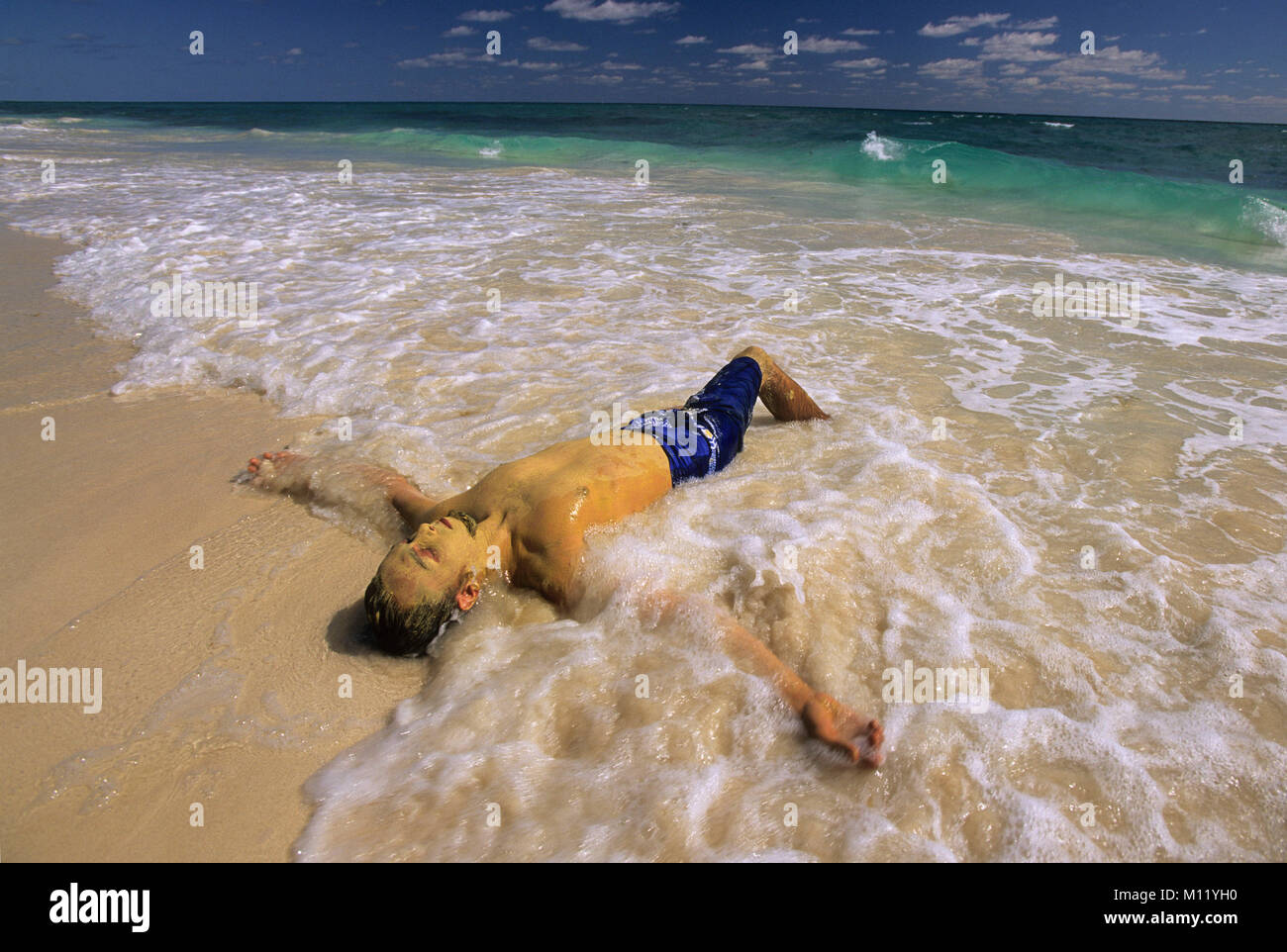 Mexico. Yucatan Peninsula. Tulum. Man lying in surf on beach washing ...