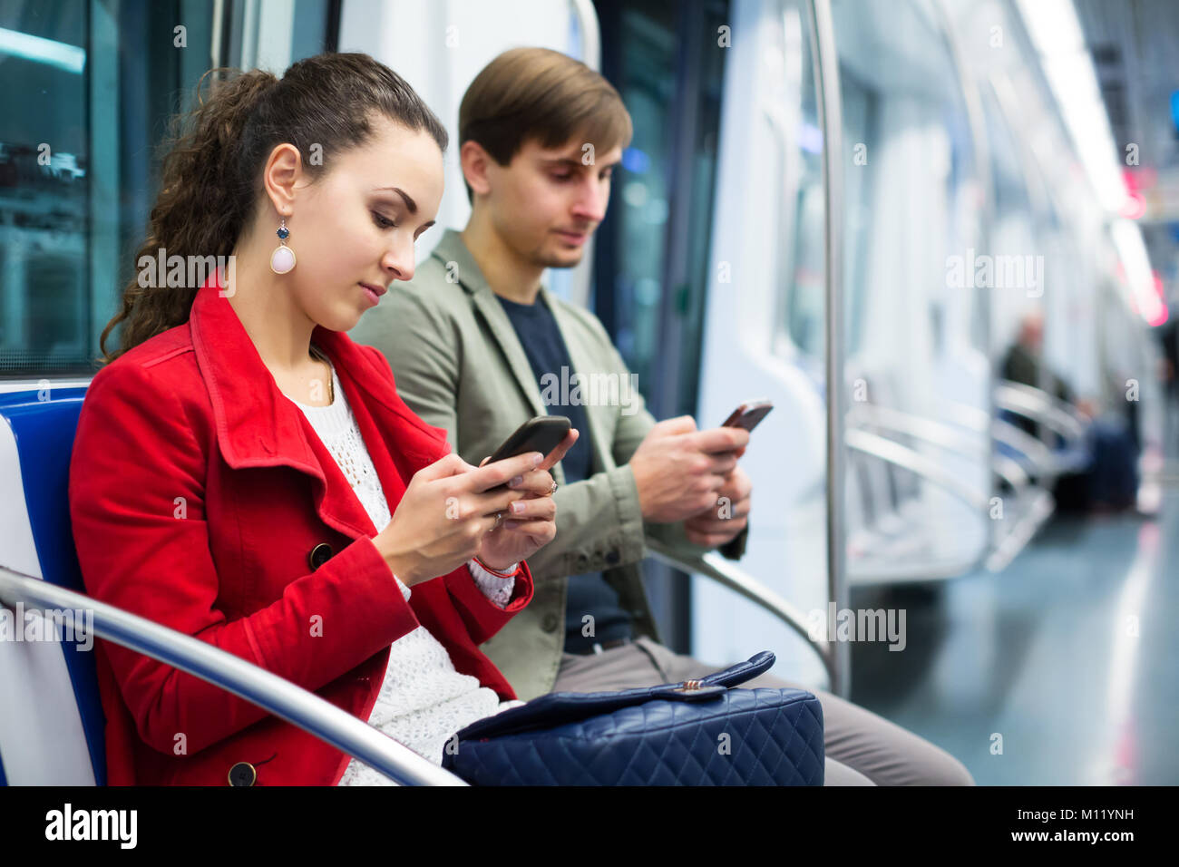 Portrait of young people reading news with mobile phones underground ...