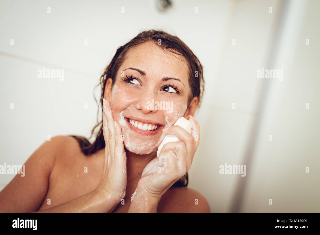 Beautiful young smiling woman washing her face with soap in the ...