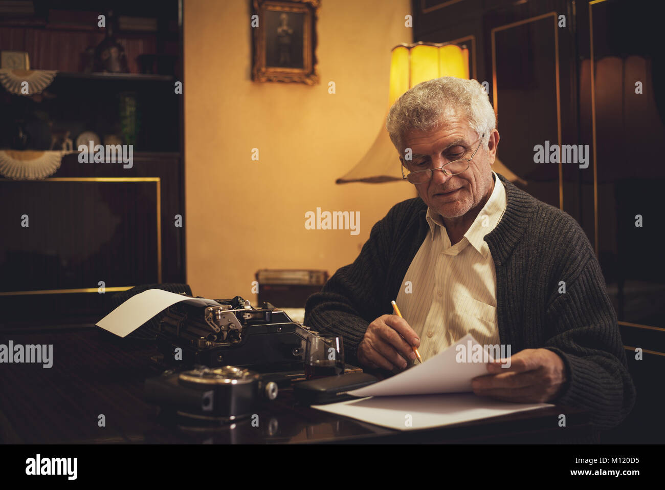 Retro senior man writer with glasses is writing with pencil beside ...