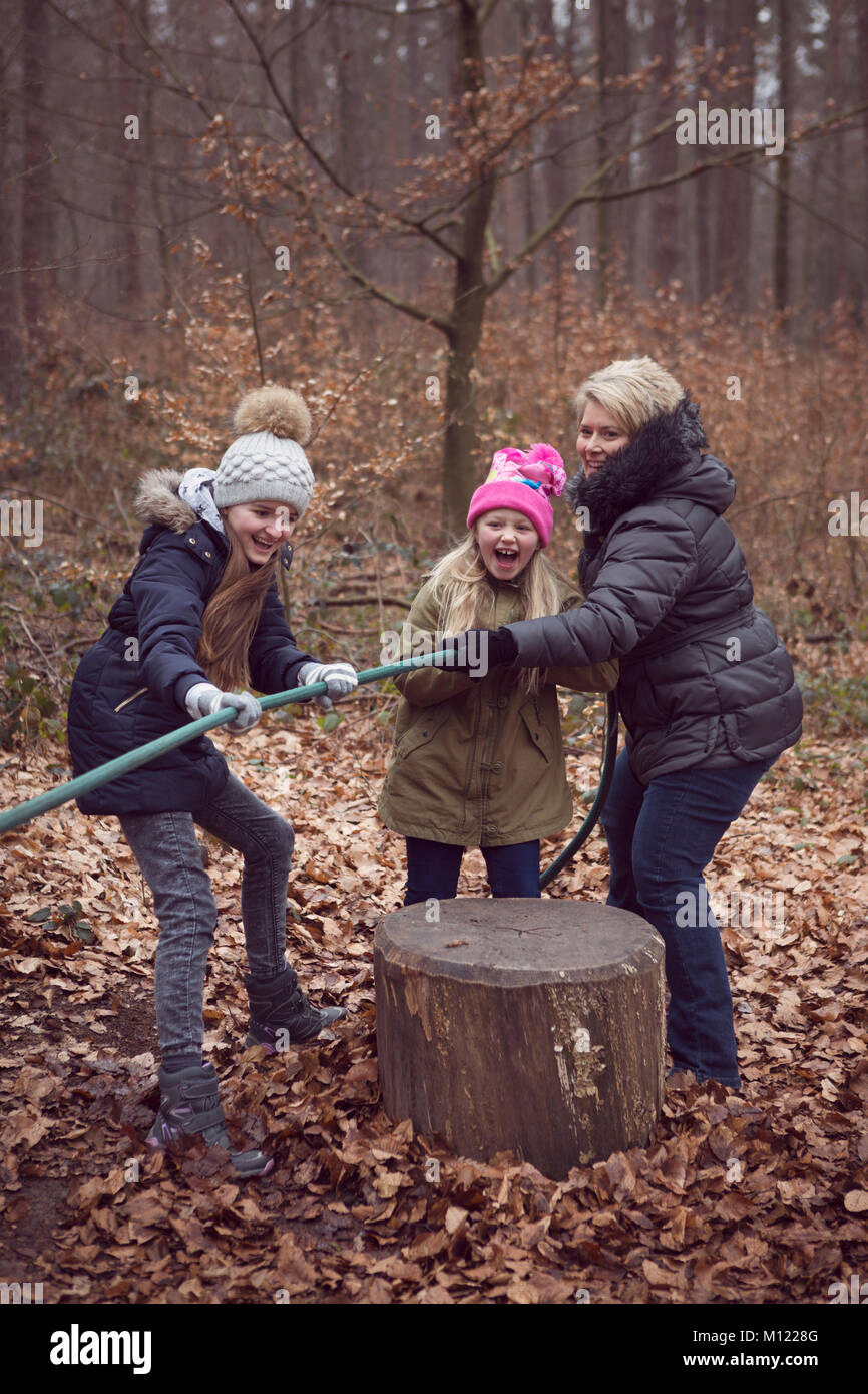 Two children and a female adult, pulling tug-of-war on a rope in ...