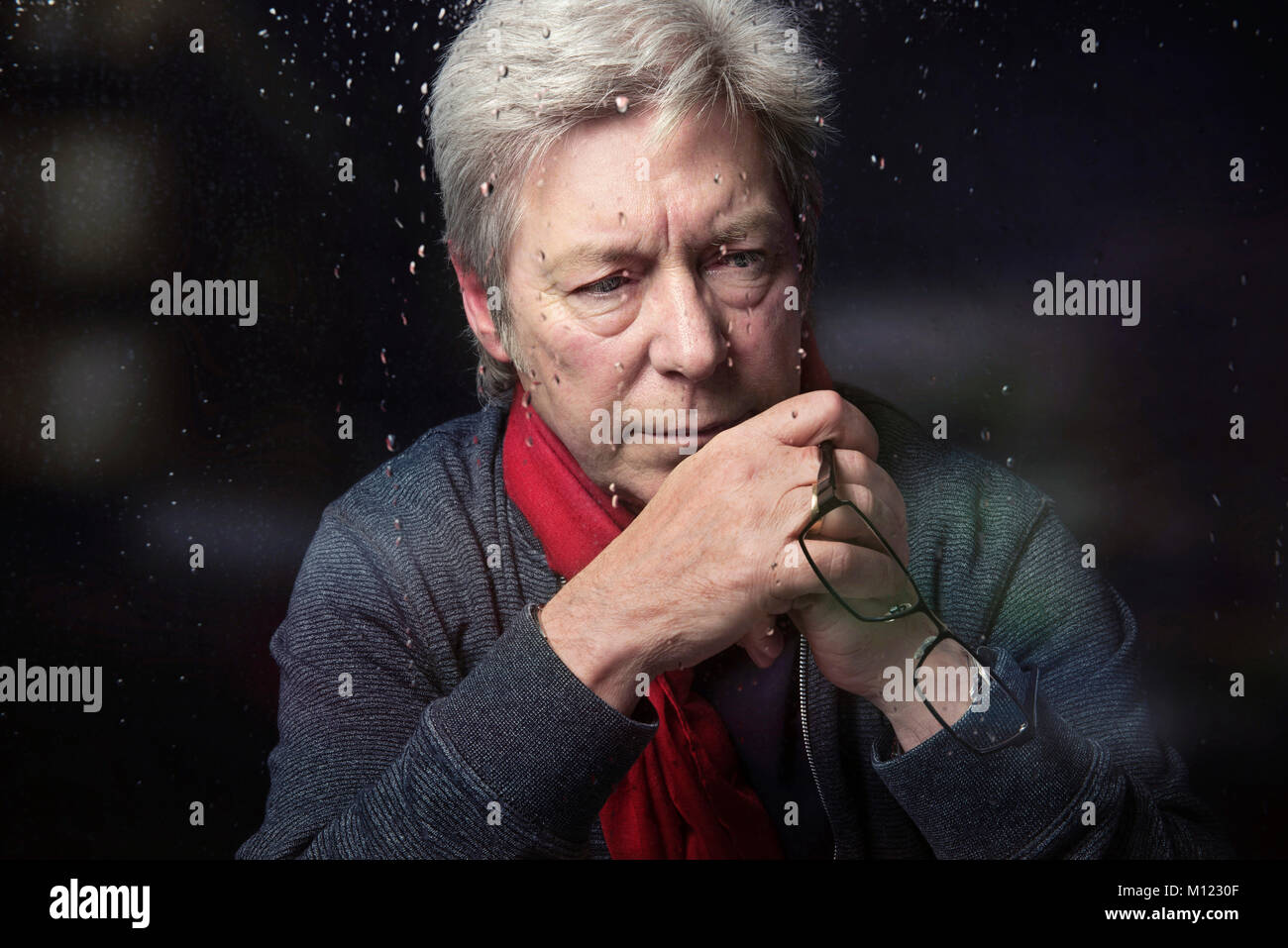 Worried man looking away holding glasses in front of face at window ...