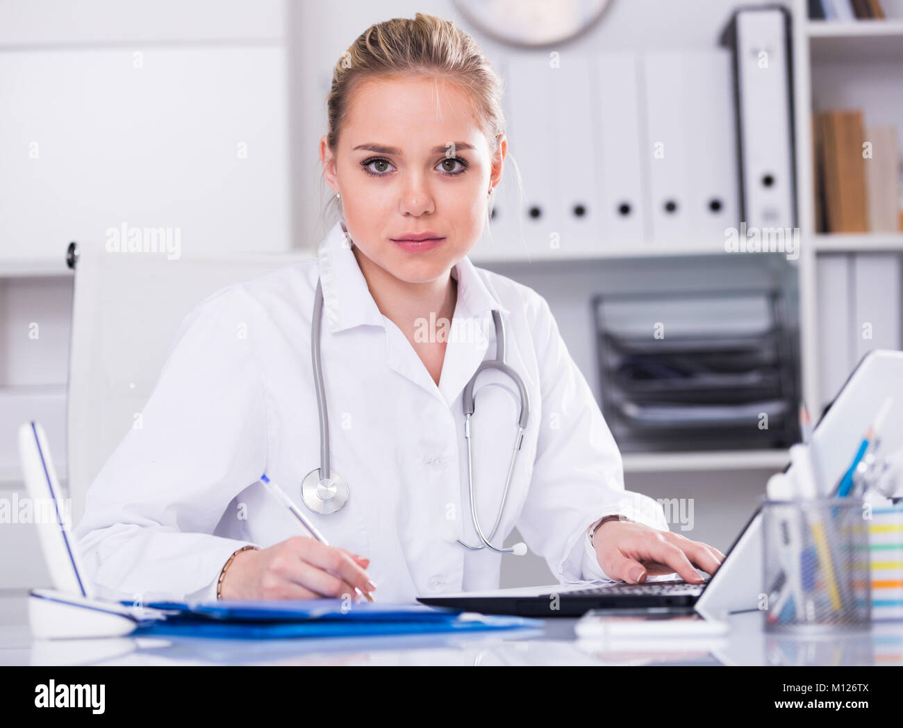 Portrait of young female doctor in white lab coat advising in medical ...