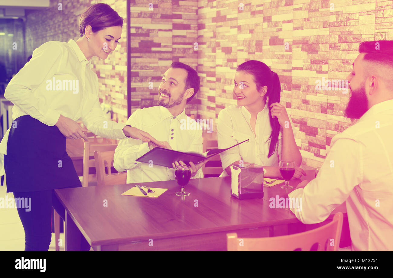 Smiling female waiter writing down order from visitors in restaurant ...
