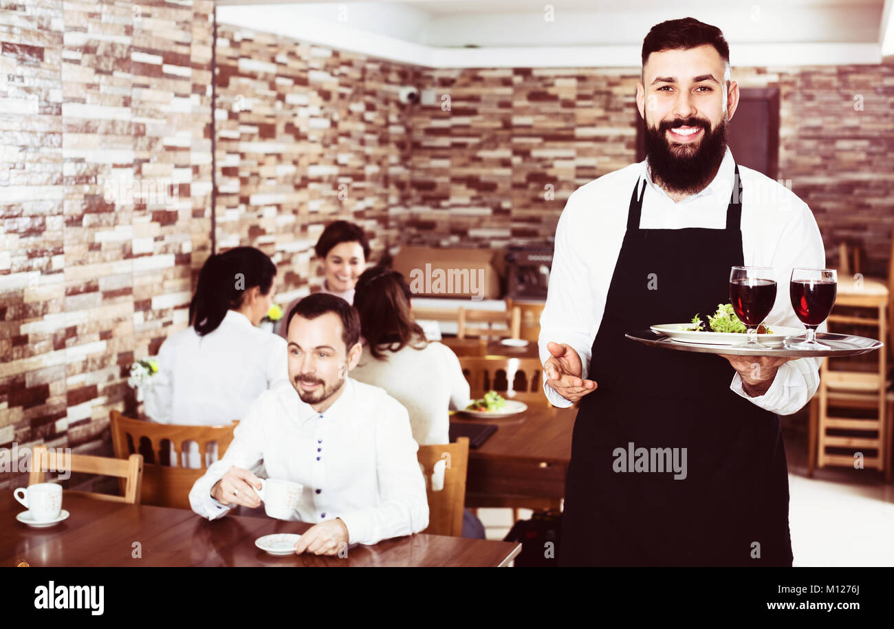 Positive male waiter showing country restaurant to visitors Stock Photo ...