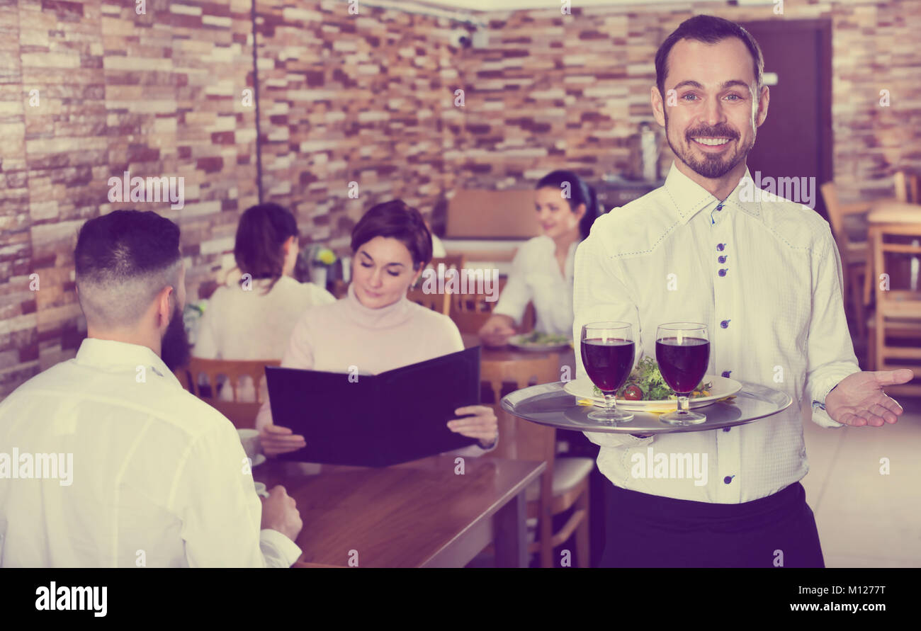 Cheerful happy waiter serving rural restaurant guests at a table Stock ...