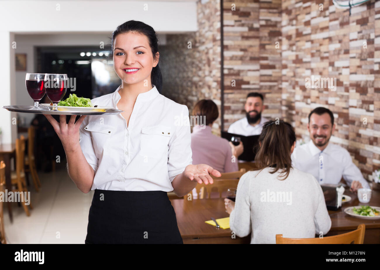 Cheerfull female waiter carrying order for visitors in country ...
