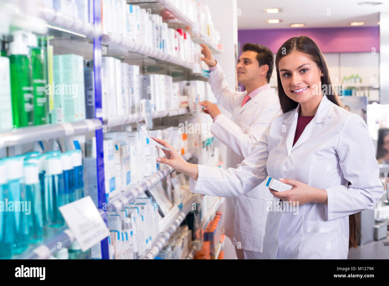 Two smiling professional pharmacists in uniform at the work in modern ...