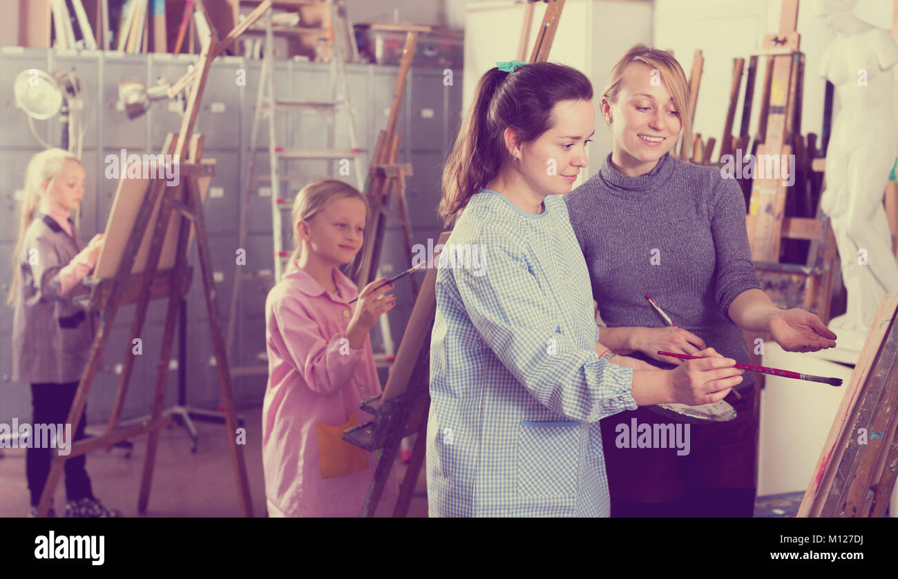 Talented female teacher helping girl during painting class at art ...