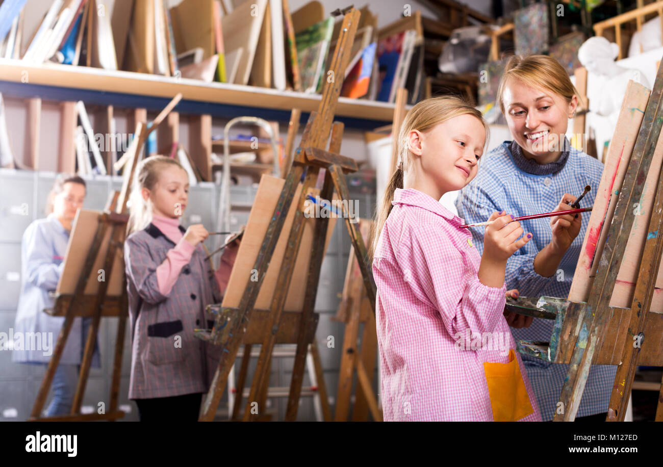 Happy female teacher helping girl during painting class at art classes ...