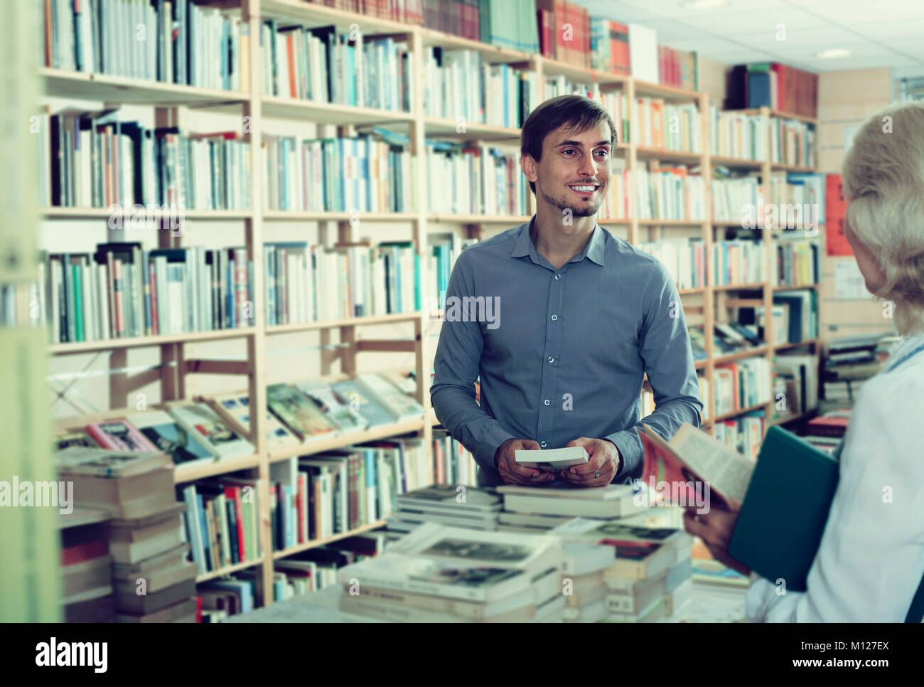 Cheerful young man seller helping customer in book store Stock Photo ...