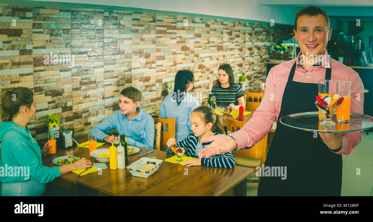 Happy young waiter serving mother with two teenage children in cafe ...