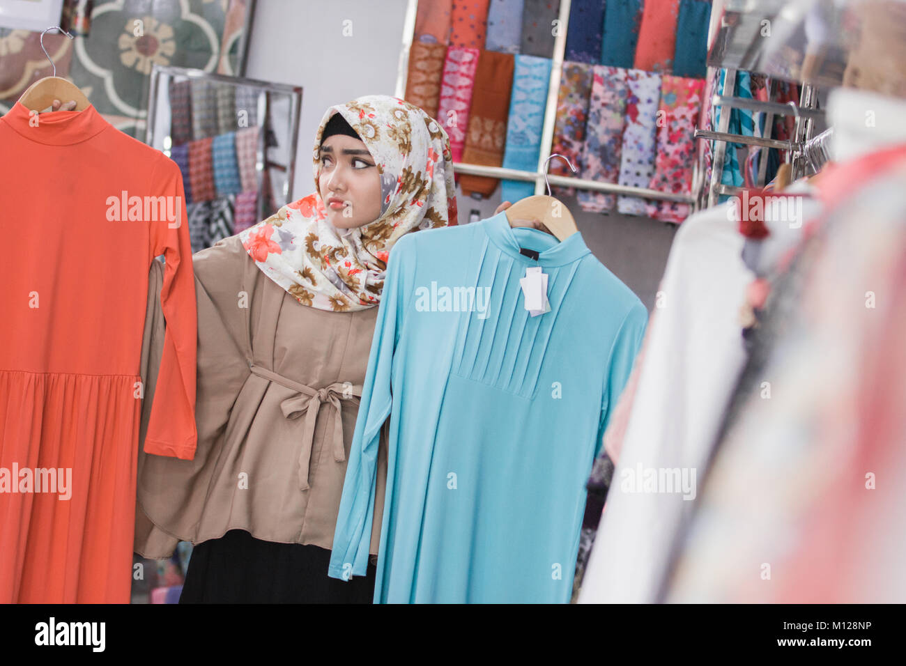 asian female confuse of choosing between two clothes in boutique ...