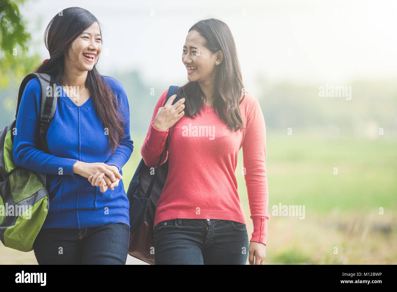 A portrait of two young Asian students chatting while walking together ...