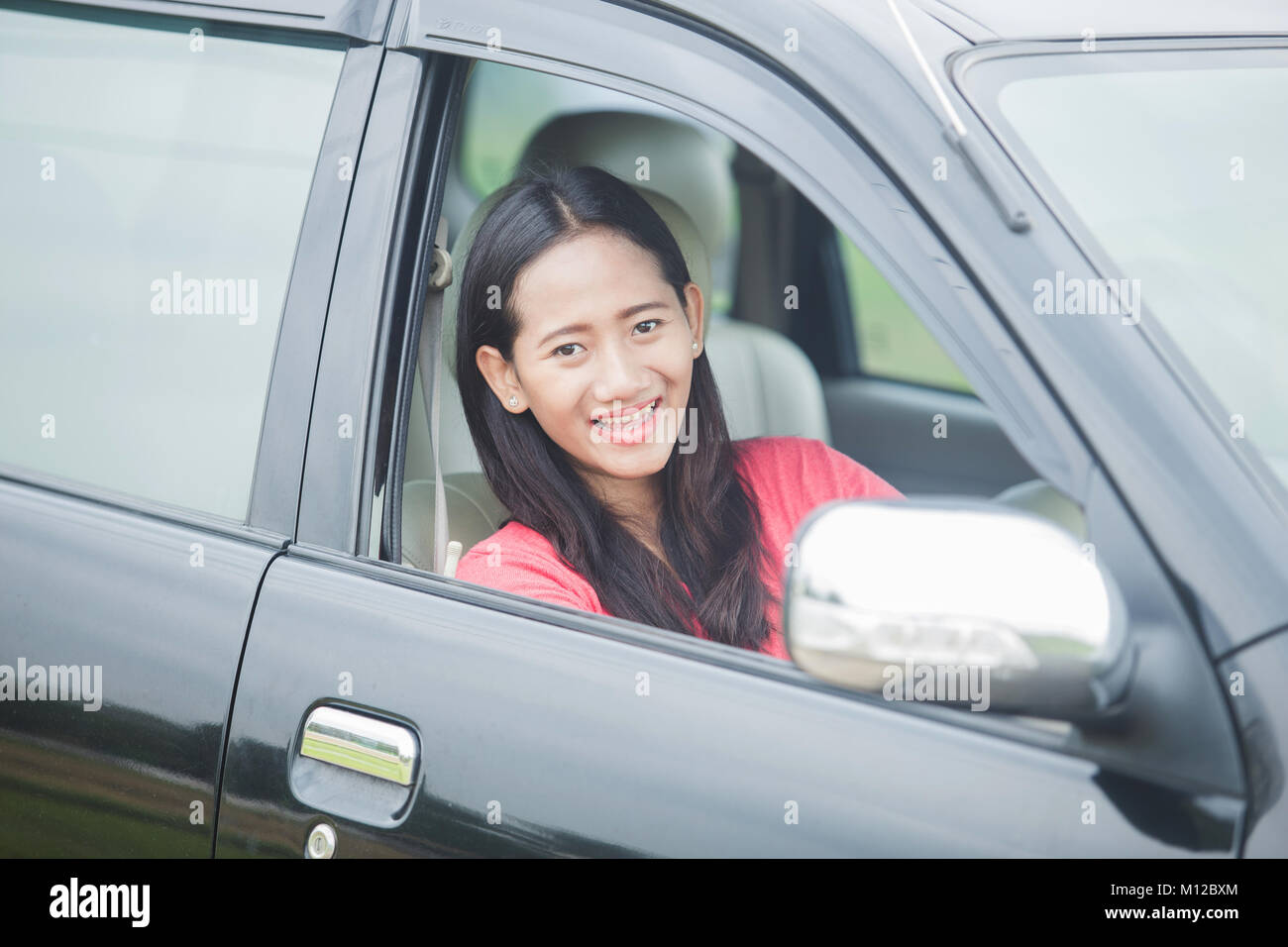 A portrait of a young Asian woman driving a car, smiling to the camera ...