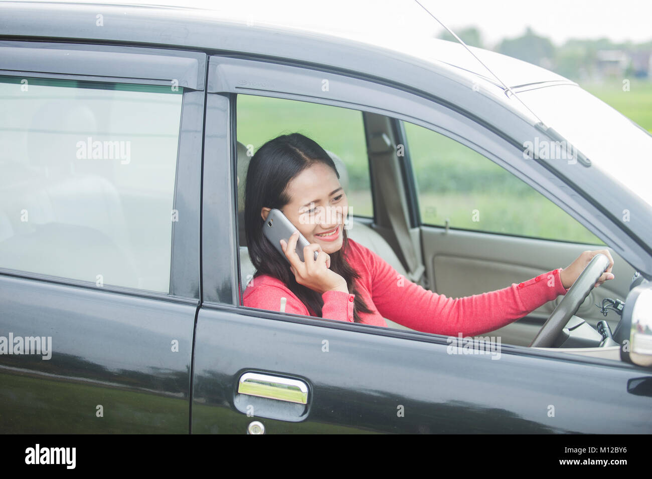 A portrait of a young Asian woman talking on the phone while driving a ...