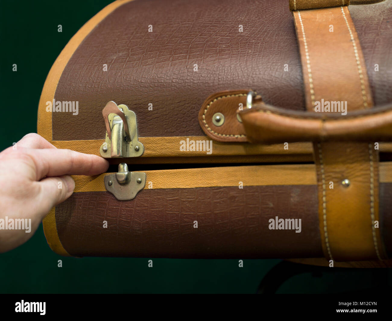 A human hand opening a lock of a looking retro suitcase, studio closeup ...