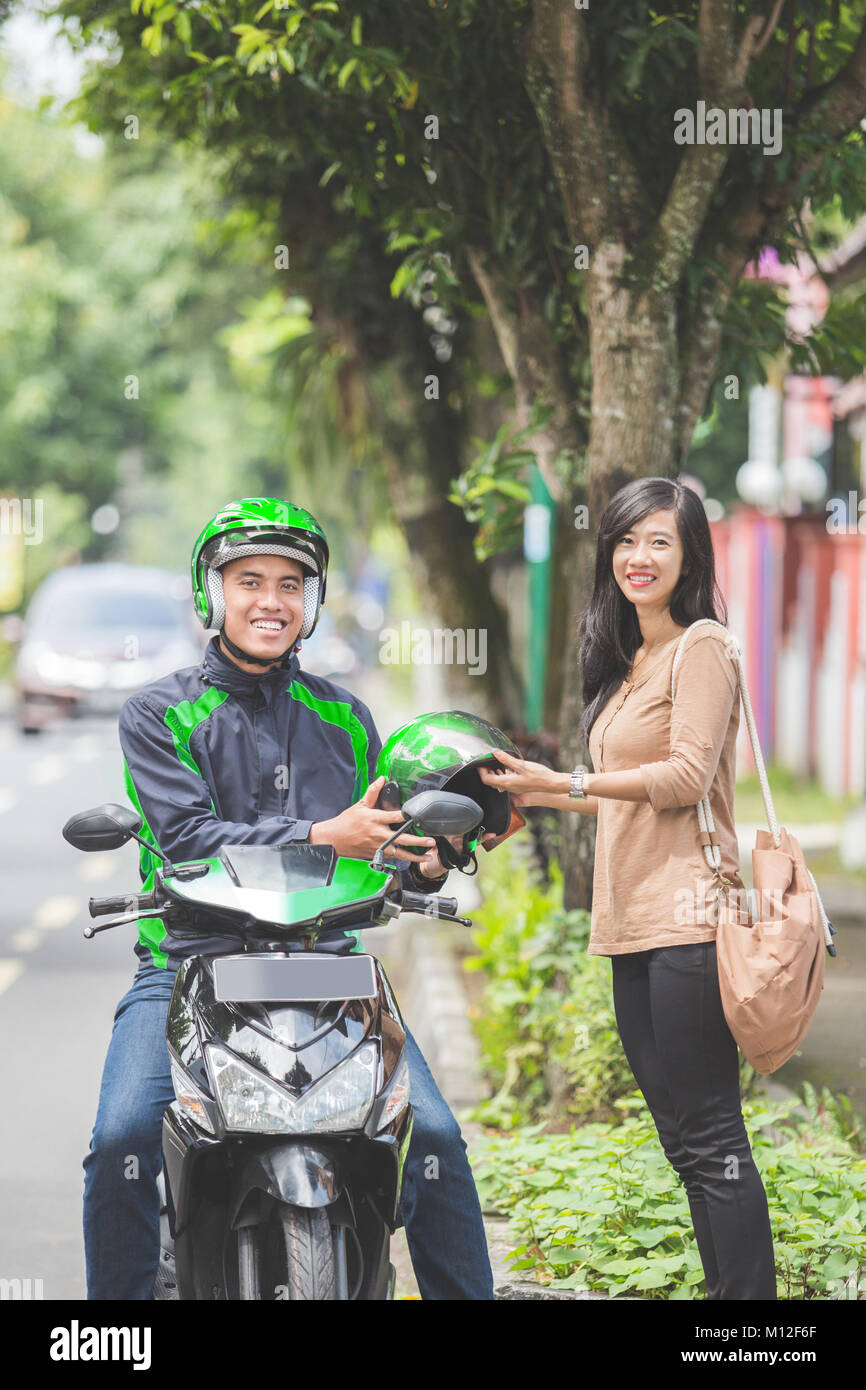 portrait of happy commercial motorcycle taxi driver giving helmet to ...