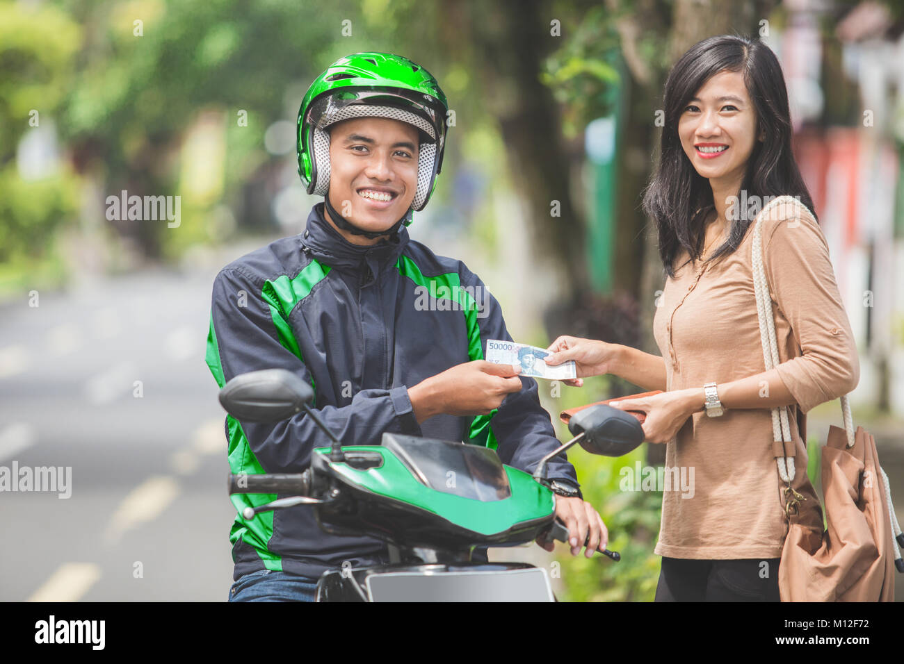 portrait of happy female customer pay for her ride to motorcycle taxi ...